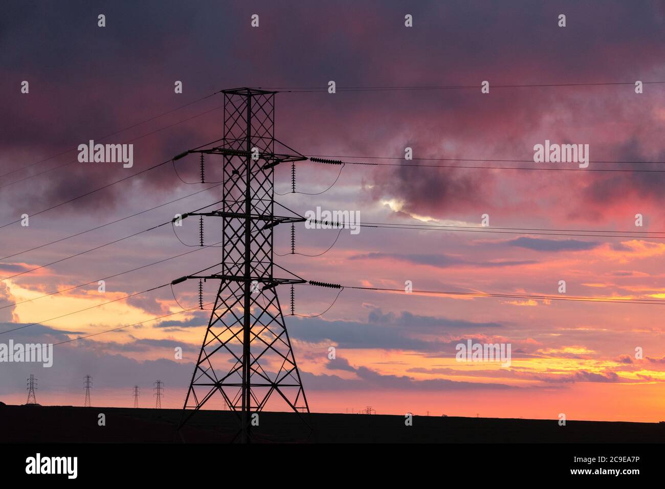 Colorful sunset and power lines and pylons in a farm rural area field ...