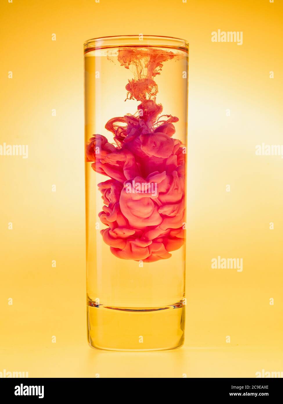 Red ink cloud in glass of water. Studio shot. Paint in water on yellow ...