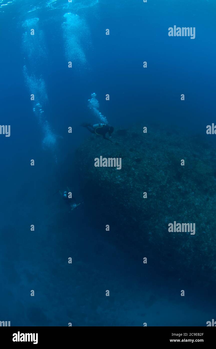 Divers swimming past rock, Pintu Kota dive site, Ambon, Indonesia ...