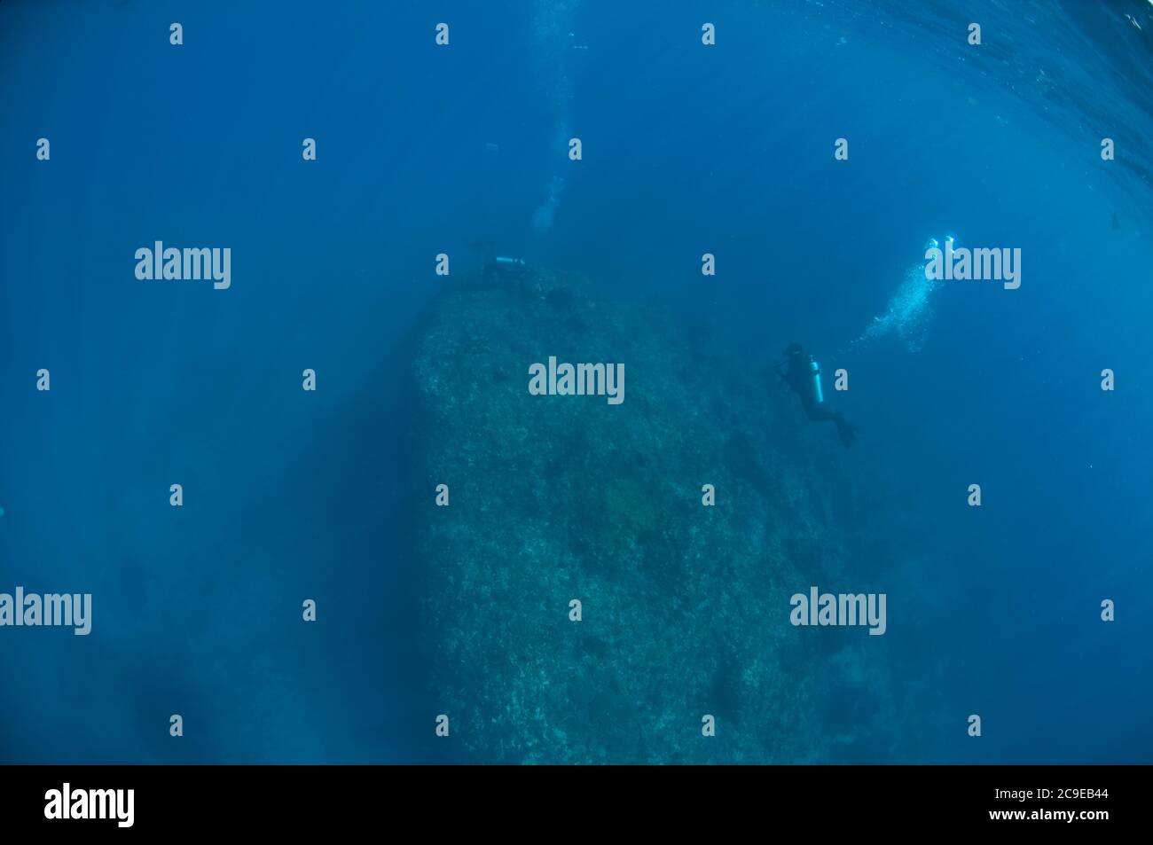Divers swimming past rock, Pintu Kota dive site, Ambon, Indonesia ...