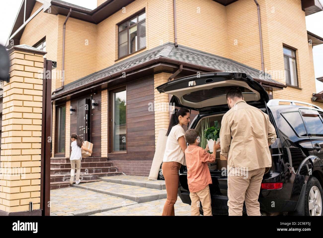 Children helping parents with unloading car and carrying moving stuff ...