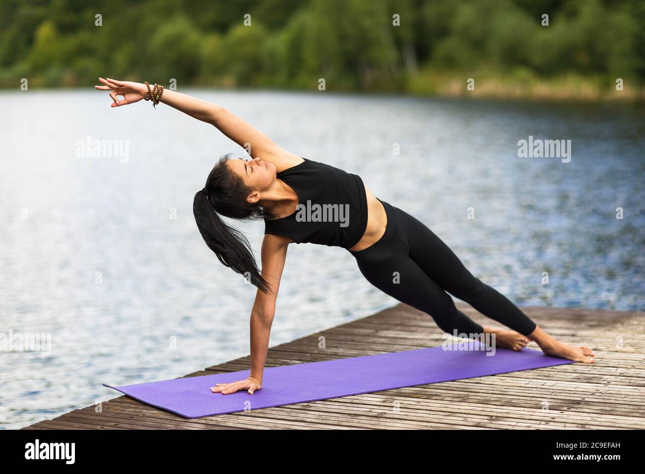 A girl on a wooden bridge near the river, practices yoga asanas ...