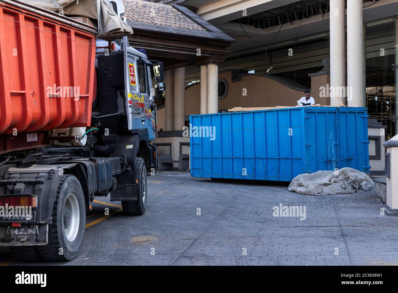 Man checking load in blue metal skip and big red lorry with silver cab ...