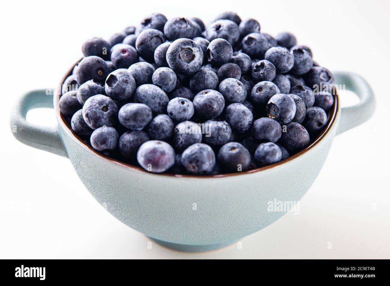 Group of ripe organic blueberries inside light blue bowl, isolates on ...