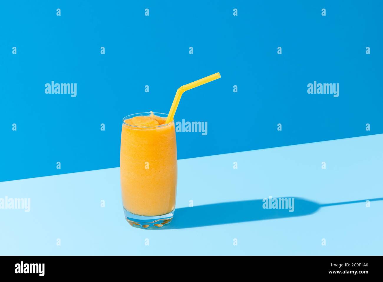 Mango milkshake with yellow straw isolated on a blue background, in ...