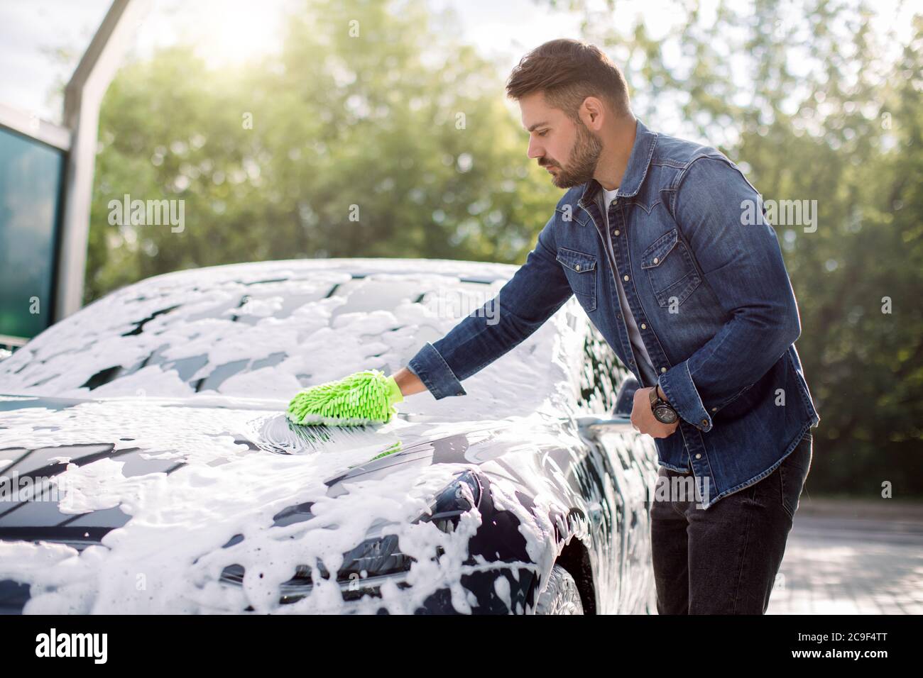 Young attractive Caucasian bearded man washing his electric luxury car ...