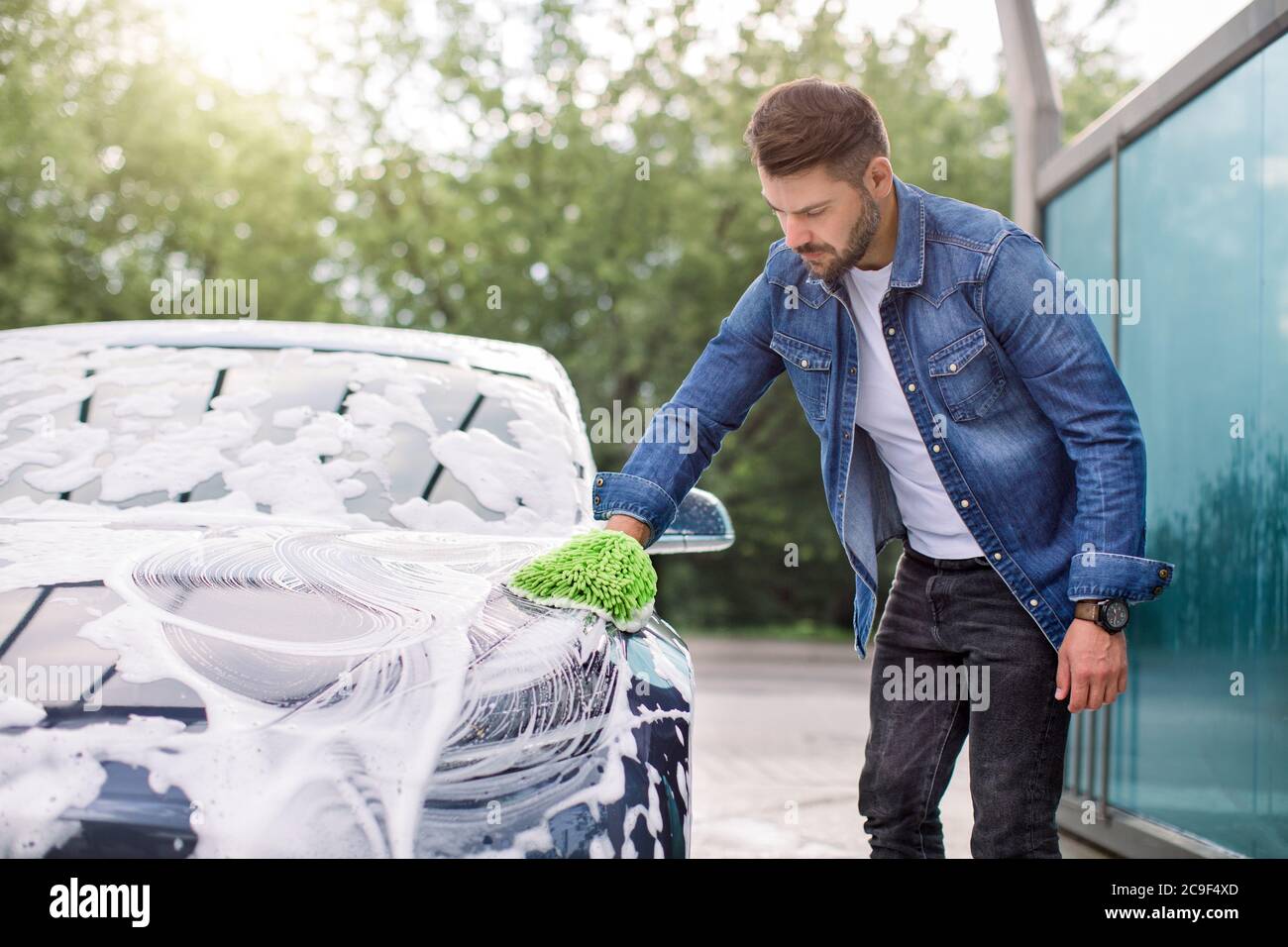 Outdoor car wash concept. Portrait of young man in casual wear, washing ...