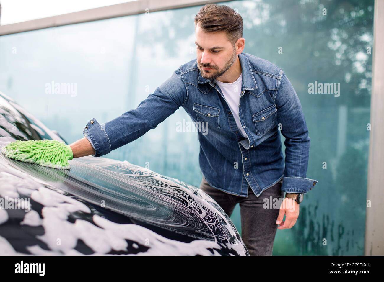 Side angle view of young handsome bearded man in jeans shirt, washing ...