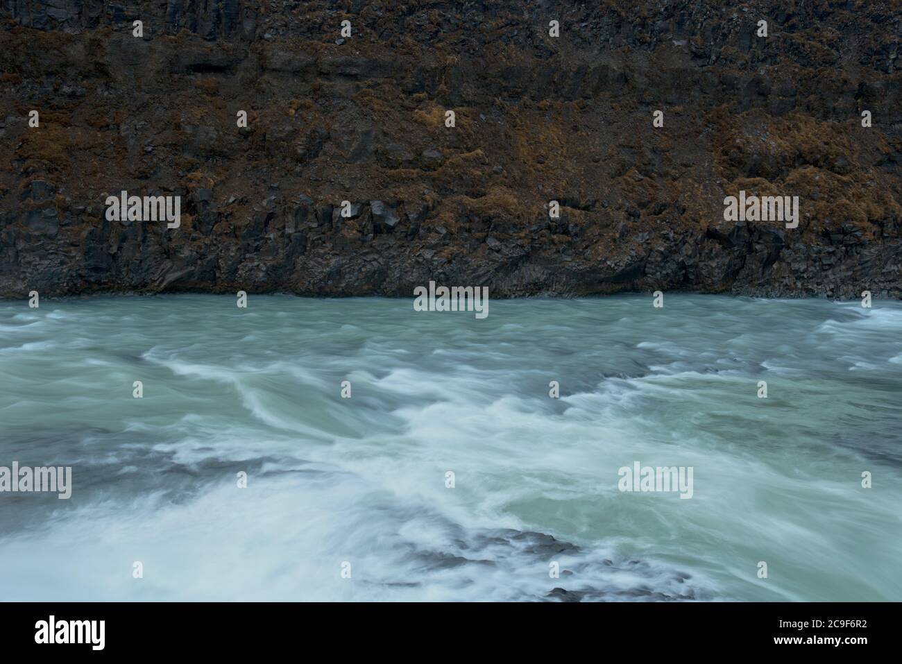 Fast flowing river with dark rocks visible just under the surface. A ...