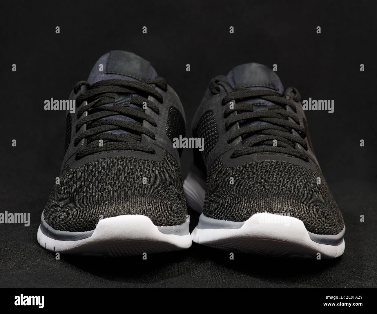 Pair of modern black running shoes front view on grey studio background ...