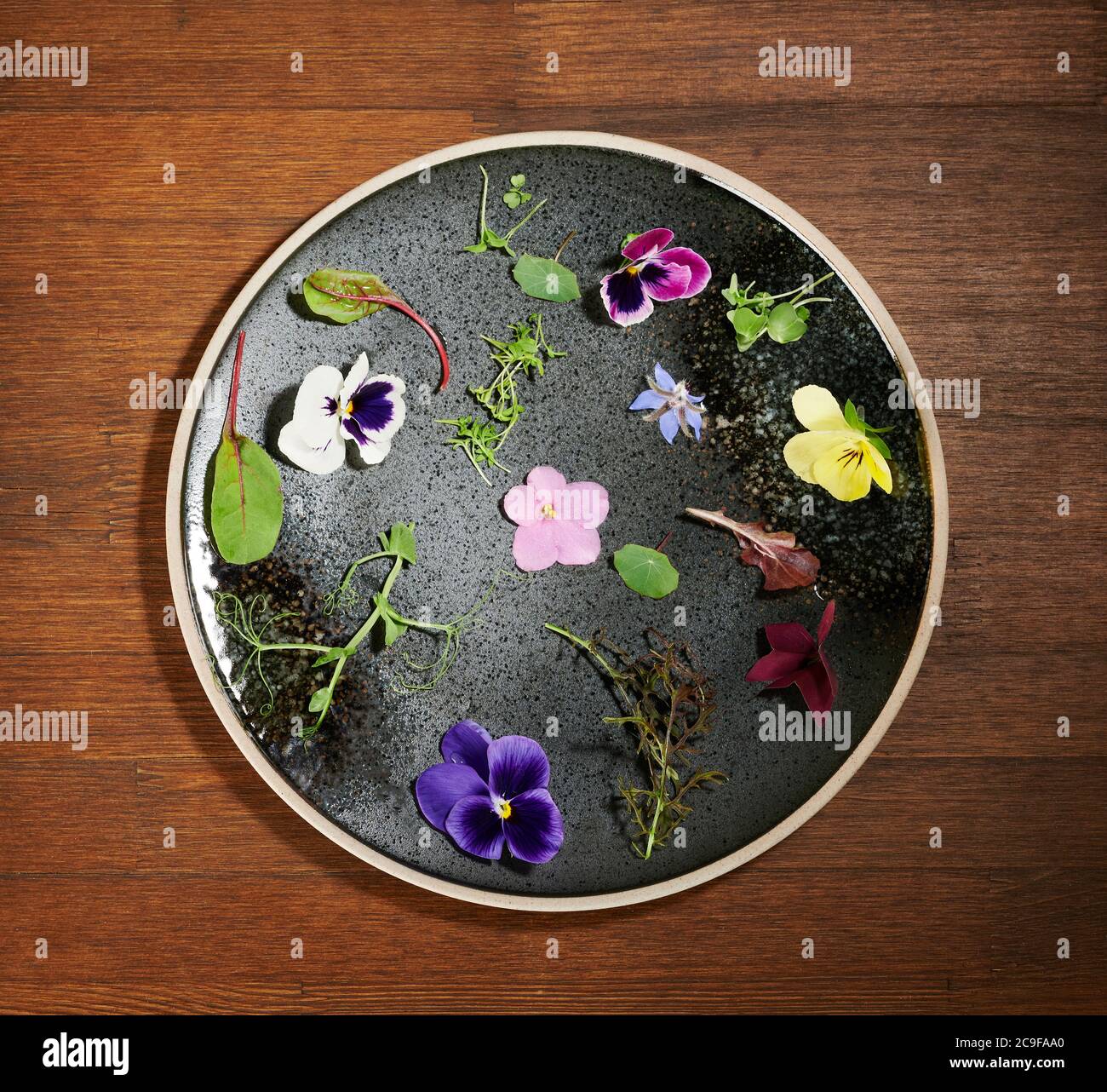 Edible plants on black plate in wooden table above top view Stock Photo ...