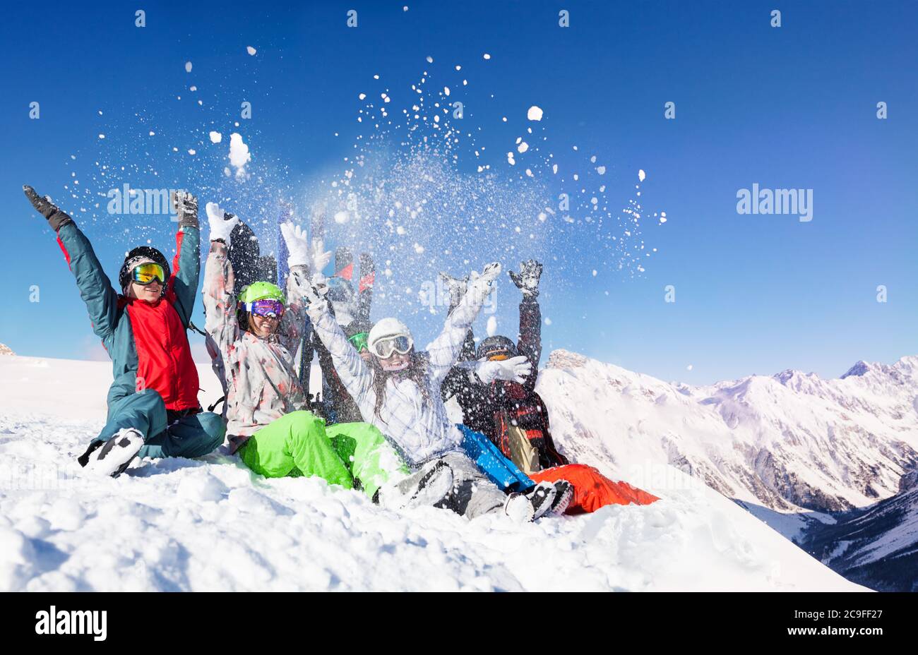 Group of young adults throw snow up in the air sitting on top of the ...