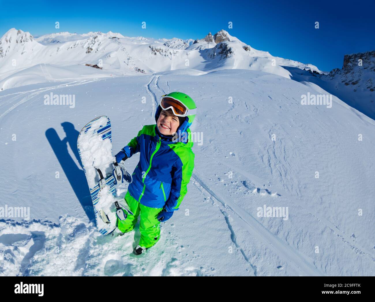 Wide mountain panorama and cute little smiling boy hold snowboard in ...