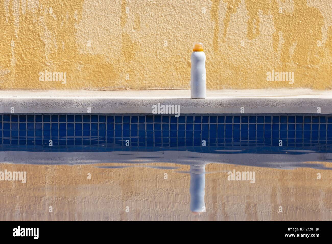 Bottle of sunscreen on the edge of a pool with the reflection in the ...