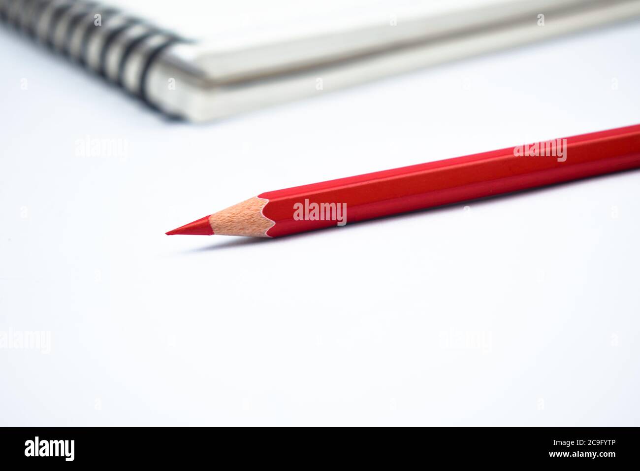 Red color wood pencil crayon placed in front of a white colored note ...