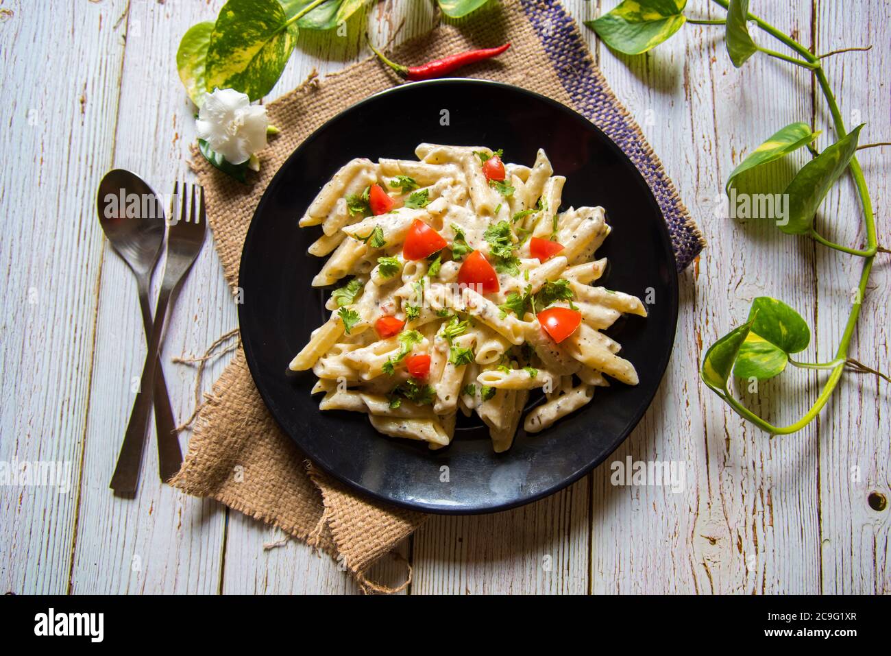 cooked penne pasta served on a black plate with condiments with use of ...