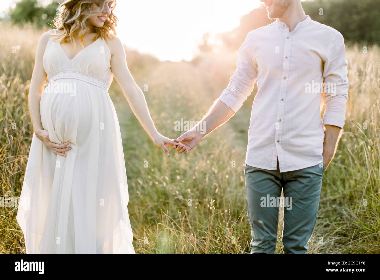 Young happy romantic pregnant couple walking in wild field in summer ...