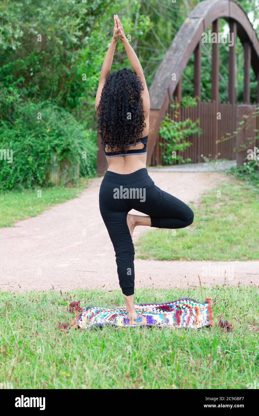 Young female of African ethnicity practicing yoga positions in the park ...