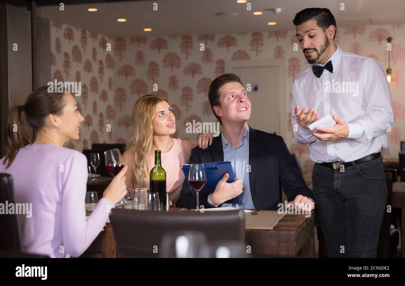 Young waiter helping group of friends with menu, taking order in ...