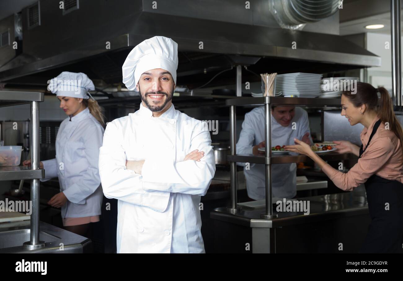 Portrait of satisfied smiling chef on restaurant kitchen with busy ...