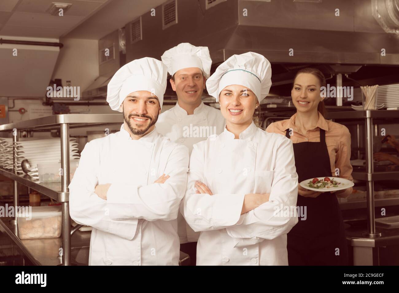 Portrait of two confident cheerful chefs in kitchen with staff of ...