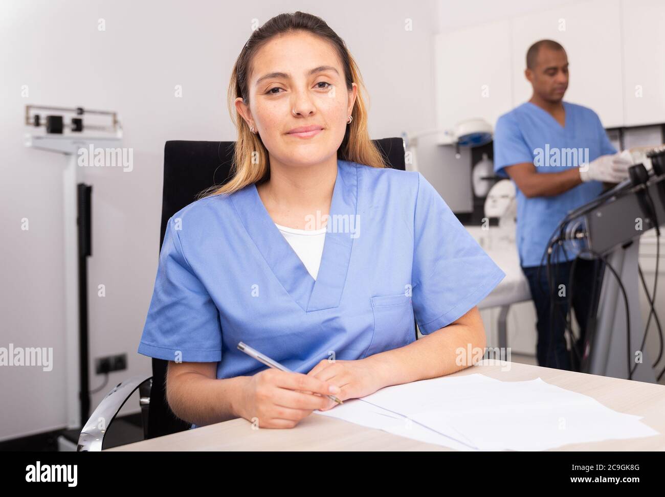 Positive female doctor cosmetologist wearing blue overall filling out ...