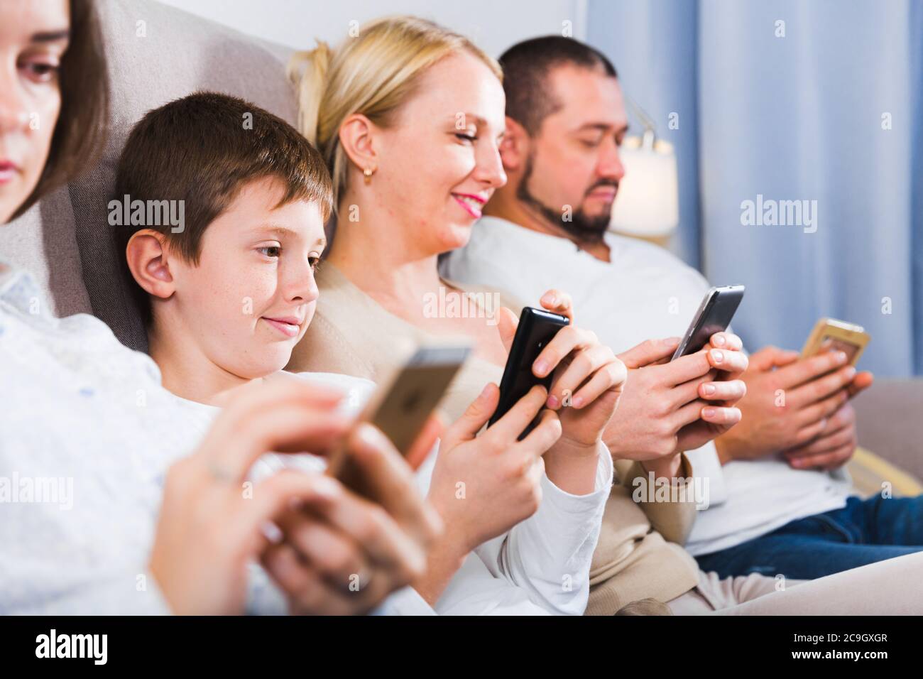 Modern young family sitting with smartphones in home interior Stock ...