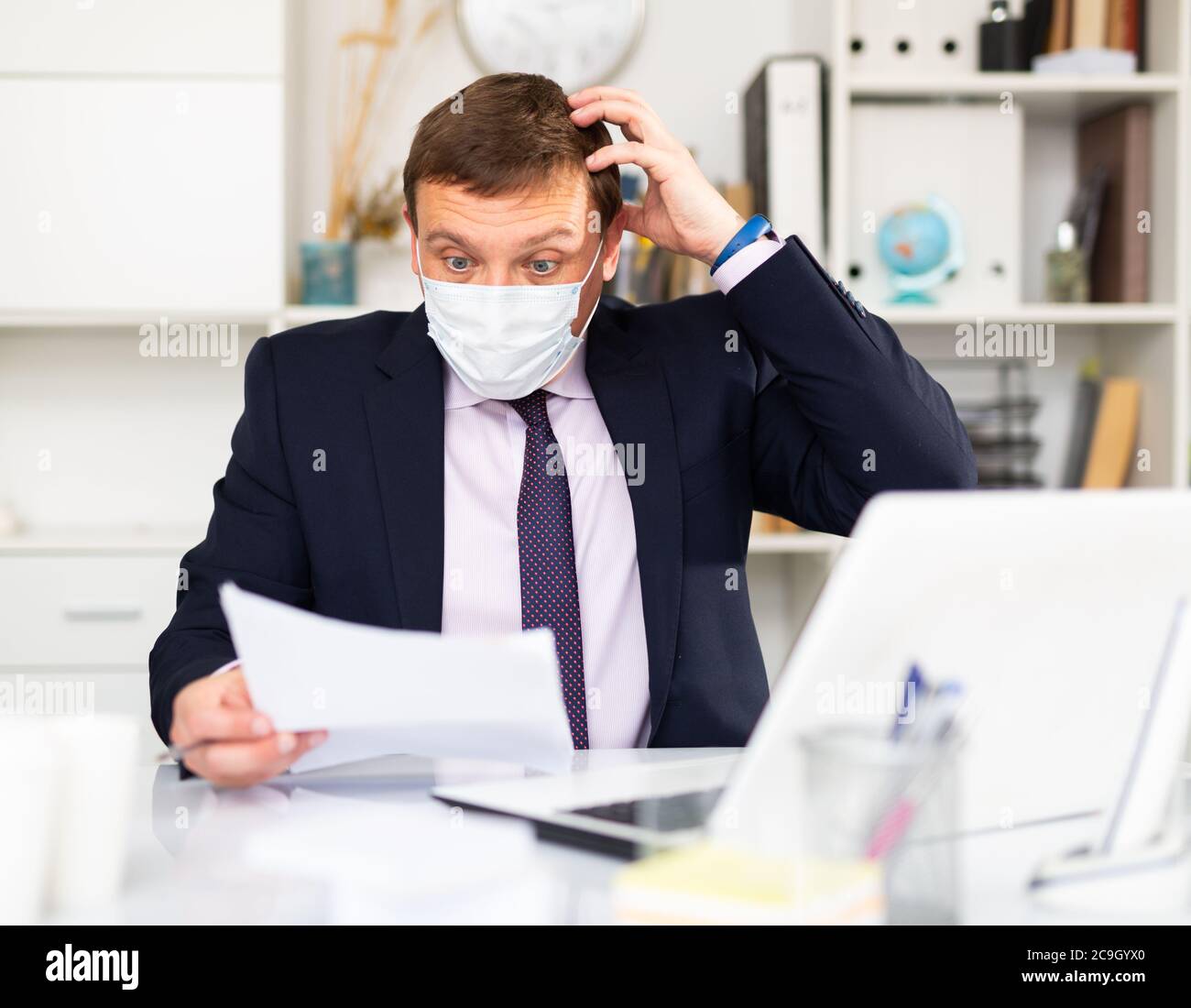 Portrait of perplexed adult man in disposable face mask working with ...
