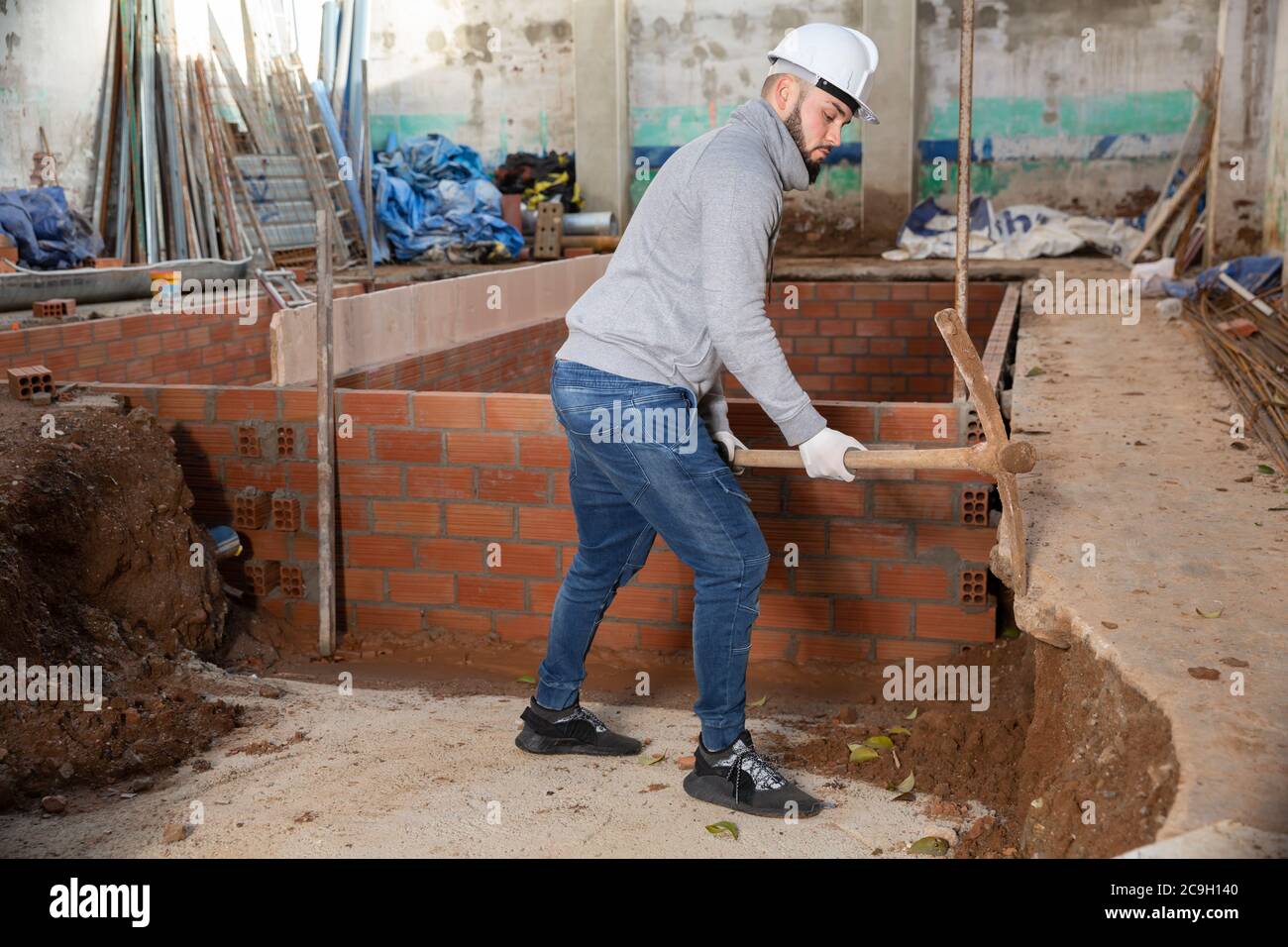 Young man digging ground with pickaxe, preparing construction pit ...