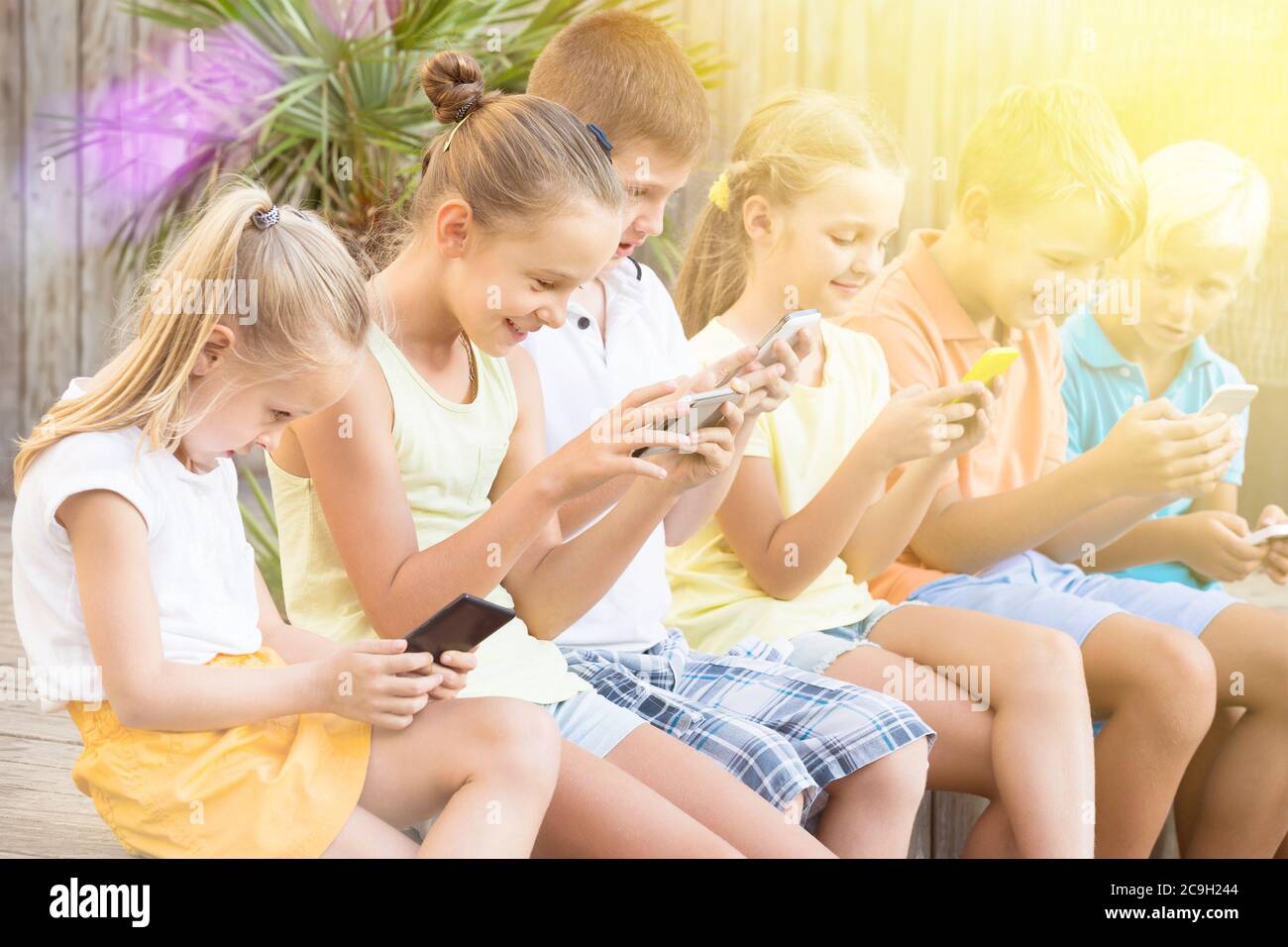 Group of friendly children playing with mobile phones together outdoors ...