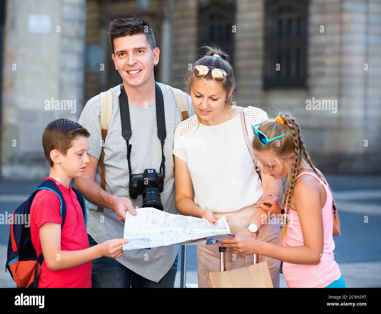Cheerful parents with two kids traveling together searching location on ...