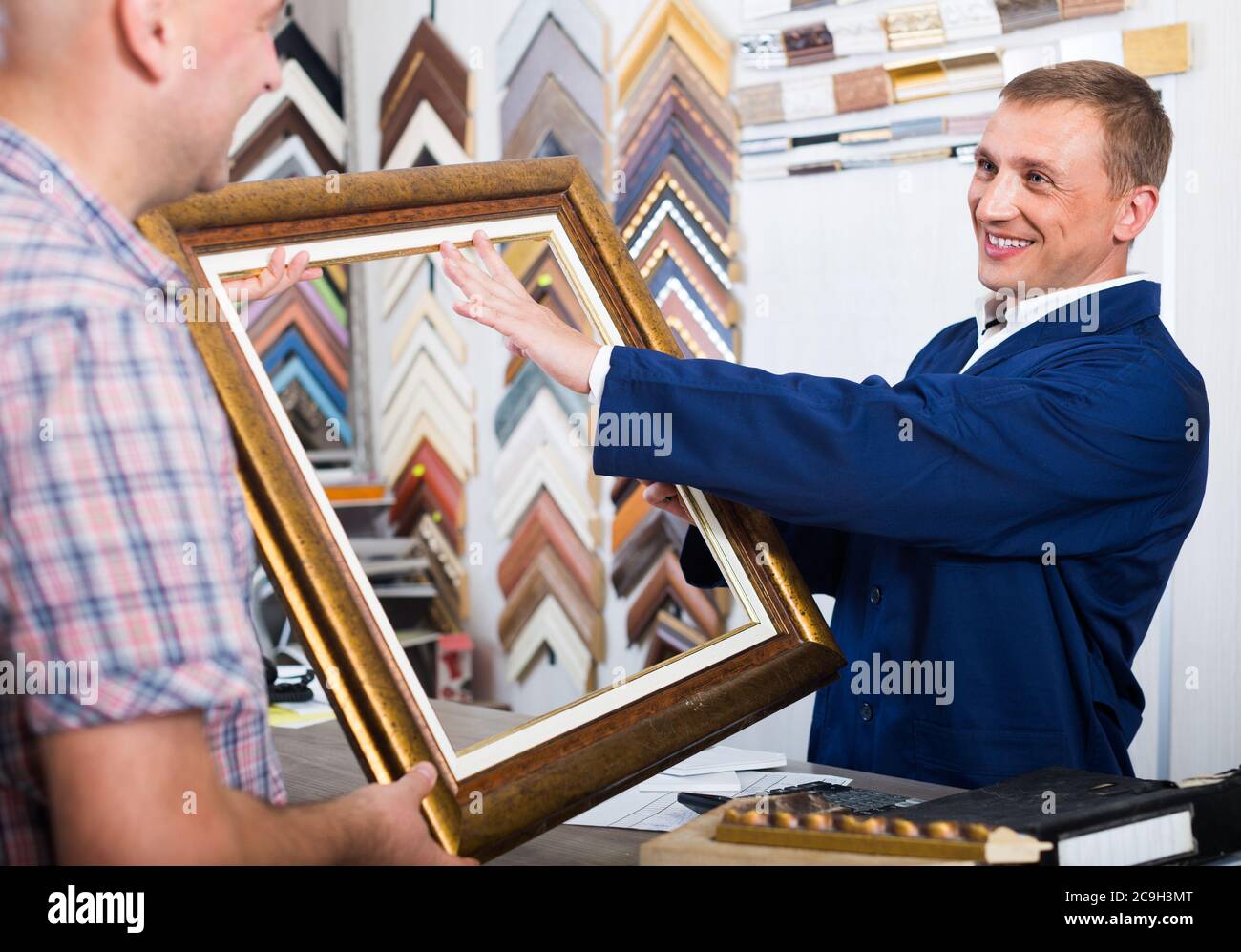 cheerful smiling man worker chatting with customer about picture frame ...