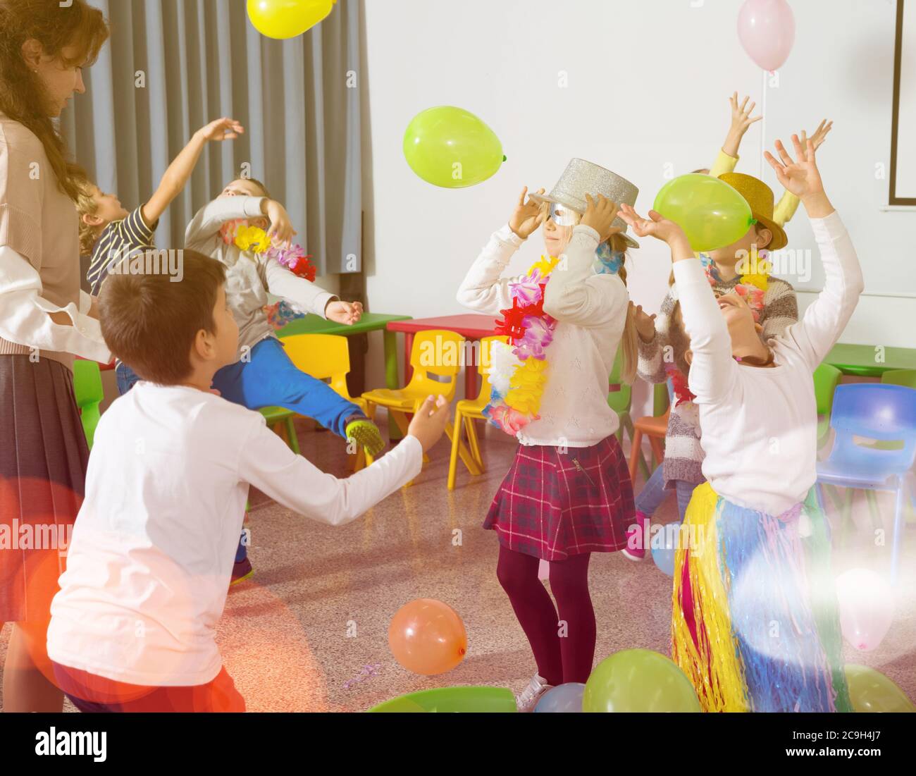 Happy kids and female teacher in funny hats and festive accessories ...