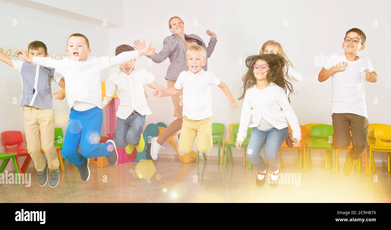 Group of happy cheerful children with their female teacher jumping ...
