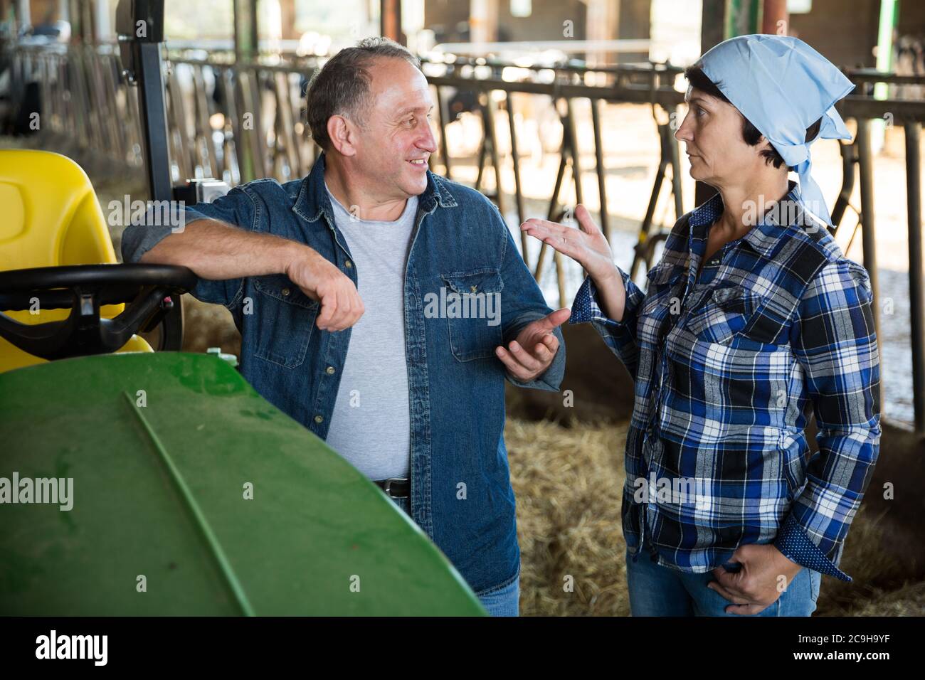 Dairy farm workers standing near tractor, communicating during break in ...