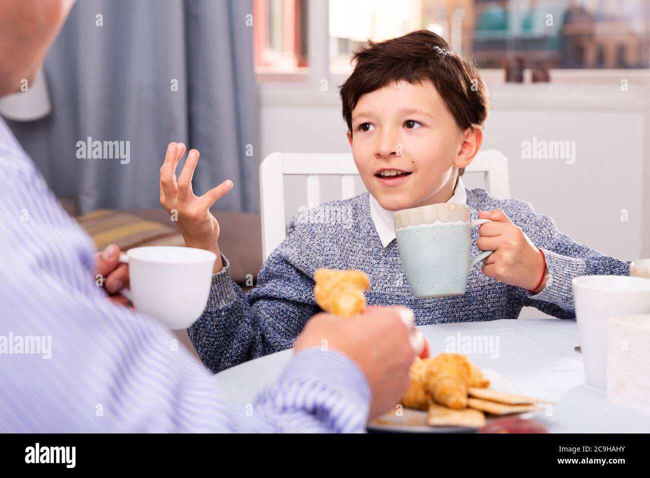 Cheerful tween boy telling interesting story to his father at home ...