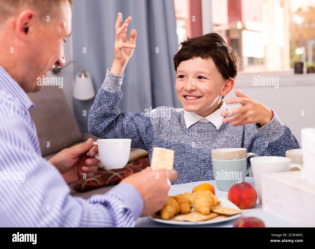 Cheerful tween boy telling interesting story to his father at home ...