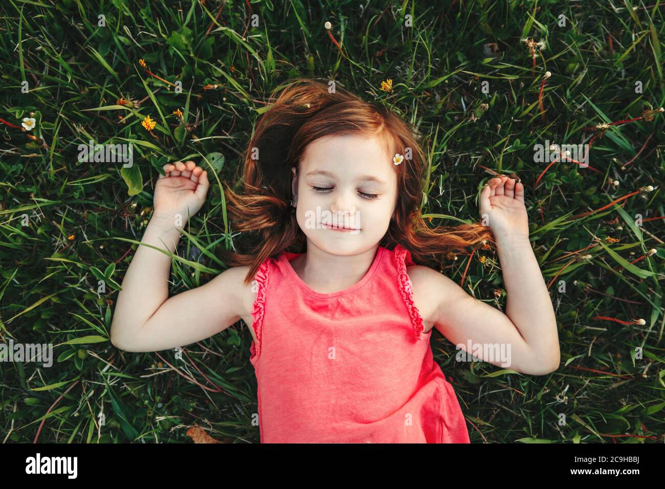Cute Caucasian girl dreaming resting in grass on meadow. Child lying ...