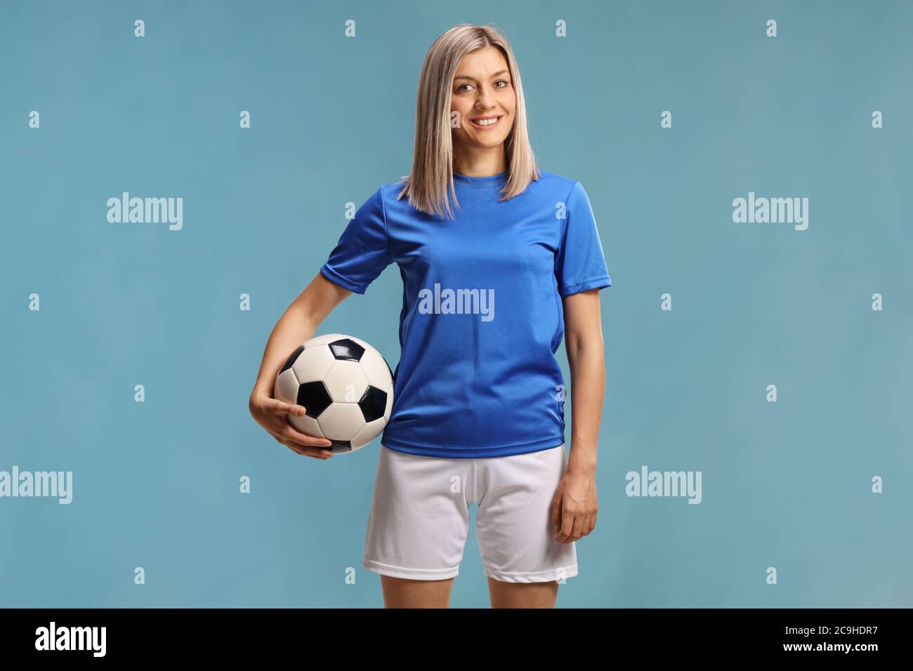 Female soccer player with a ball under arm isolated on blue background ...