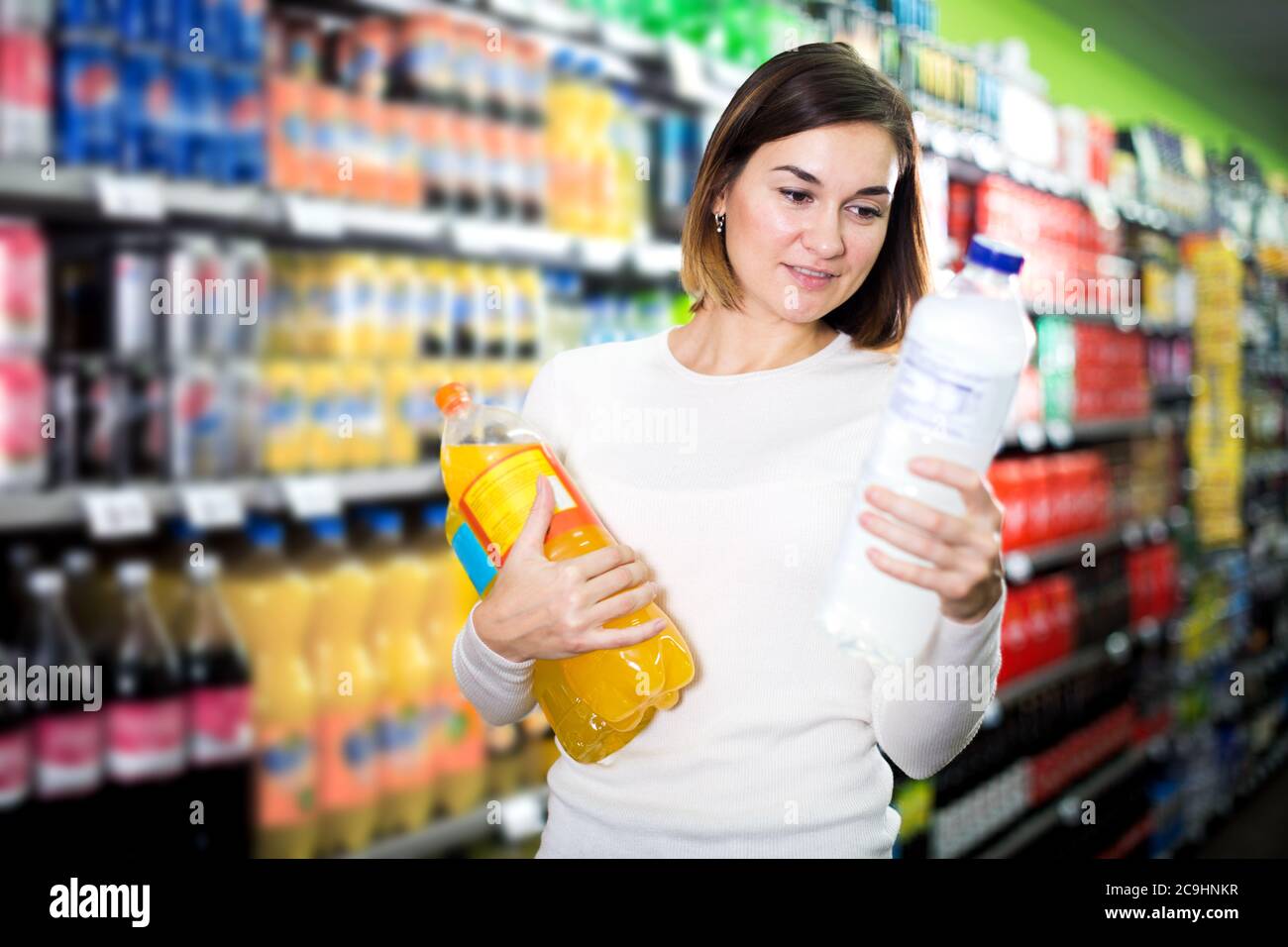 Pretty young female shopper searching for beverages in supermarket ...