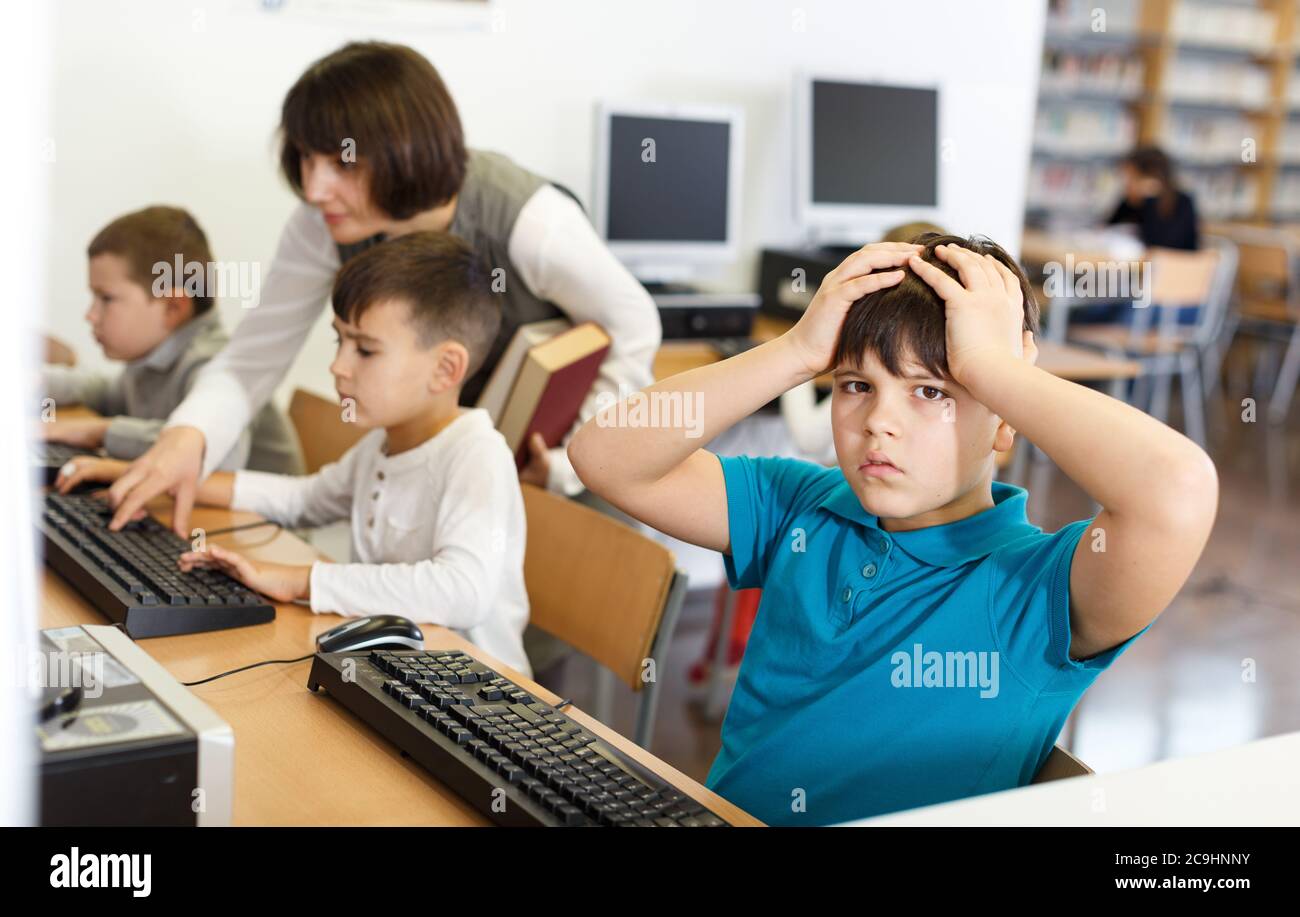 Worried upset boy sitting in computer class of school library on ...