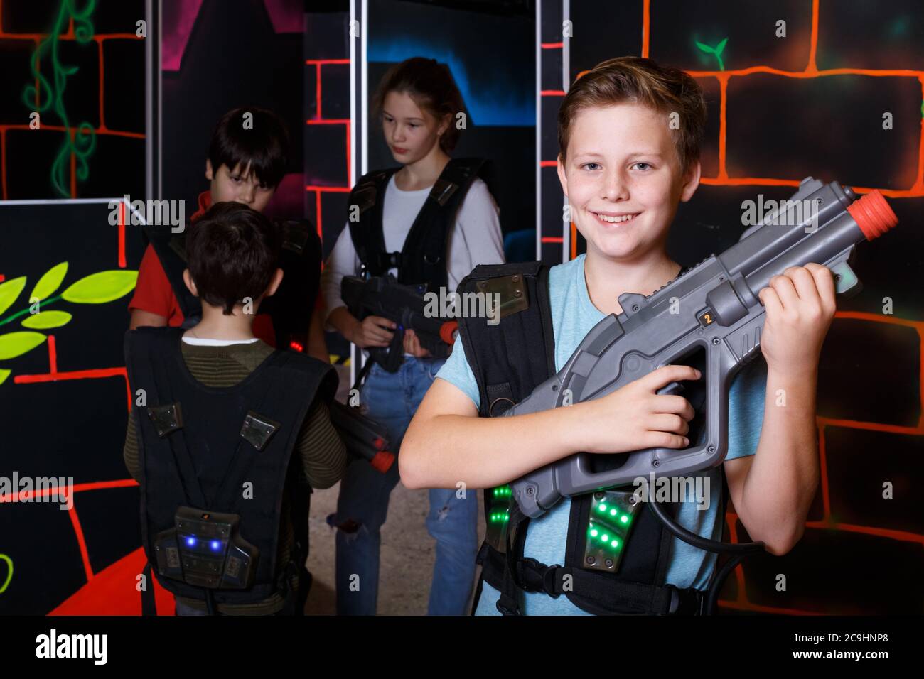 Portrait of laughing boy standing with laser gun on dark lasertag arena ...