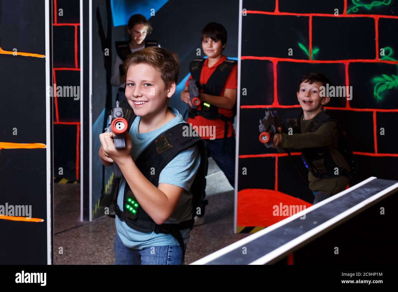 Excited boy aiming laser gun at other players during lasertag game in ...