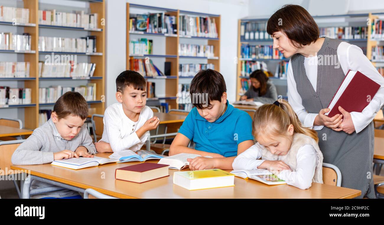 Group of cheerful school kids studying in school library with friendly ...