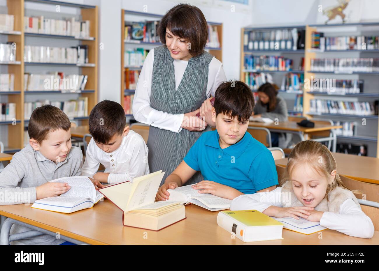 Group of school kids studying in school library with friendly female ...