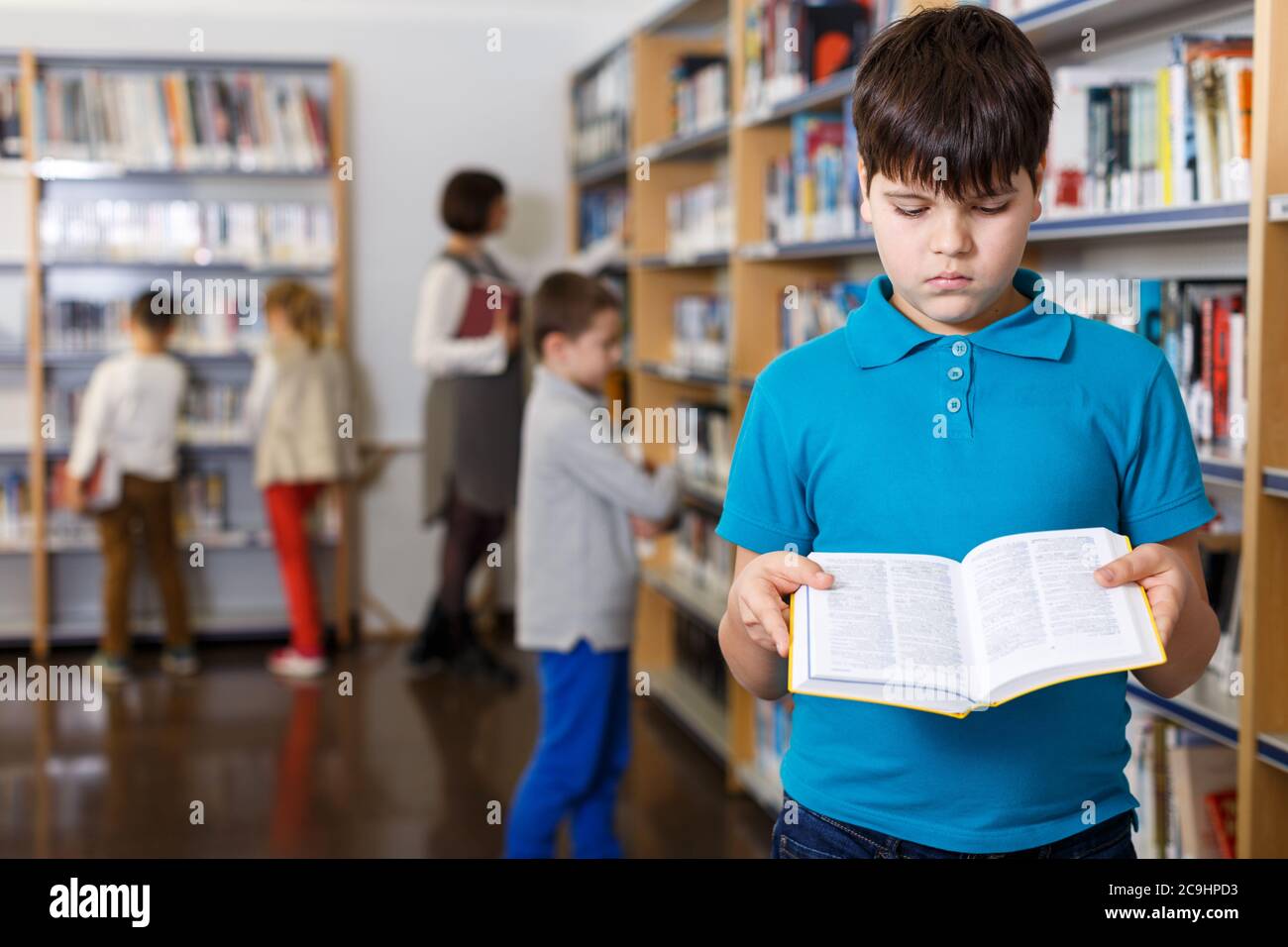 Portrait of upset tween boy browsing book in school library Stock Photo ...