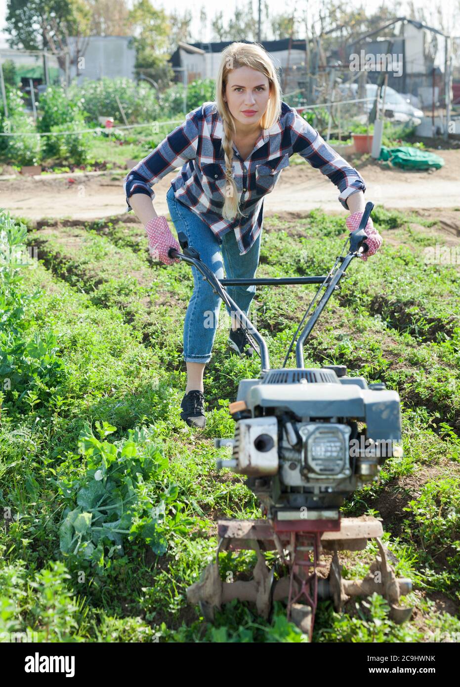 Young woman gardener using plow at land with green grass in garden ...