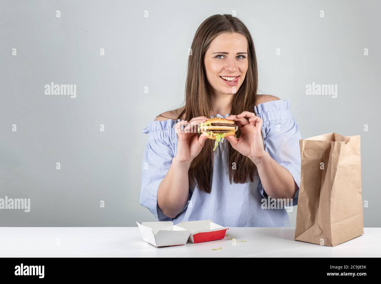 Portrait of a beautiful young woman eating a burger, isolated on white ...