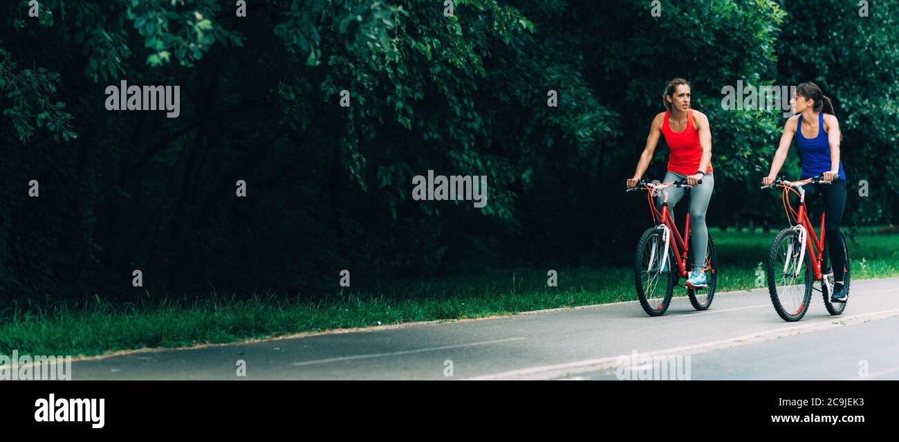 Female friends riding bikes together in park Stock Photo - Alamy