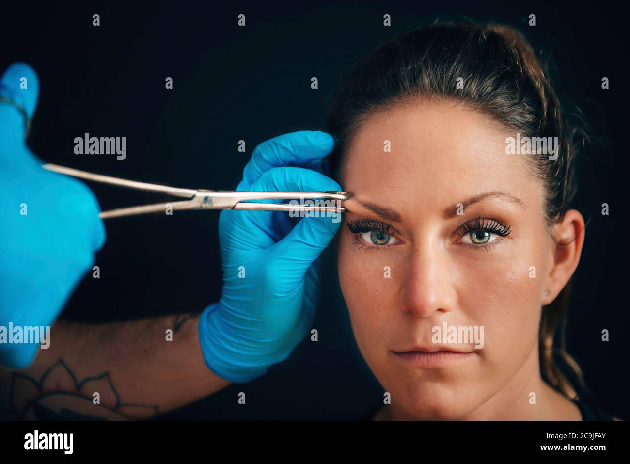 Portrait of a beautiful young woman getting her eyebrow pierced, body ...